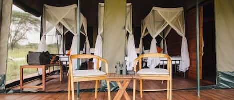 Acomodação em tenda com duas cadeiras de madeira e uma mesa, mosquiteiros e vista para o exterior.