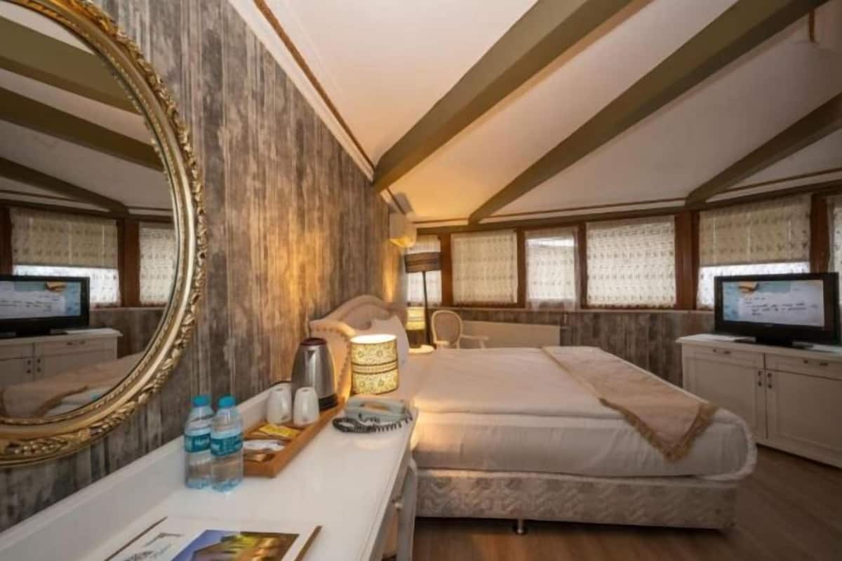Quarto de hotel com uma cama grande, escrivaninha com espelho, televisão e janela com cortinas.