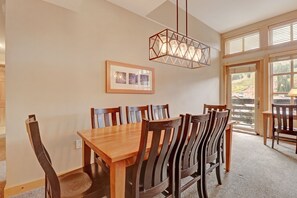 Uma sala de jantar com uma mesa e cadeiras de madeira, um lustre pendurado e um quadro na parede.