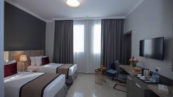 Quarto de hotel com duas camas, uma escrivaninha, televisão e área de refeições.
