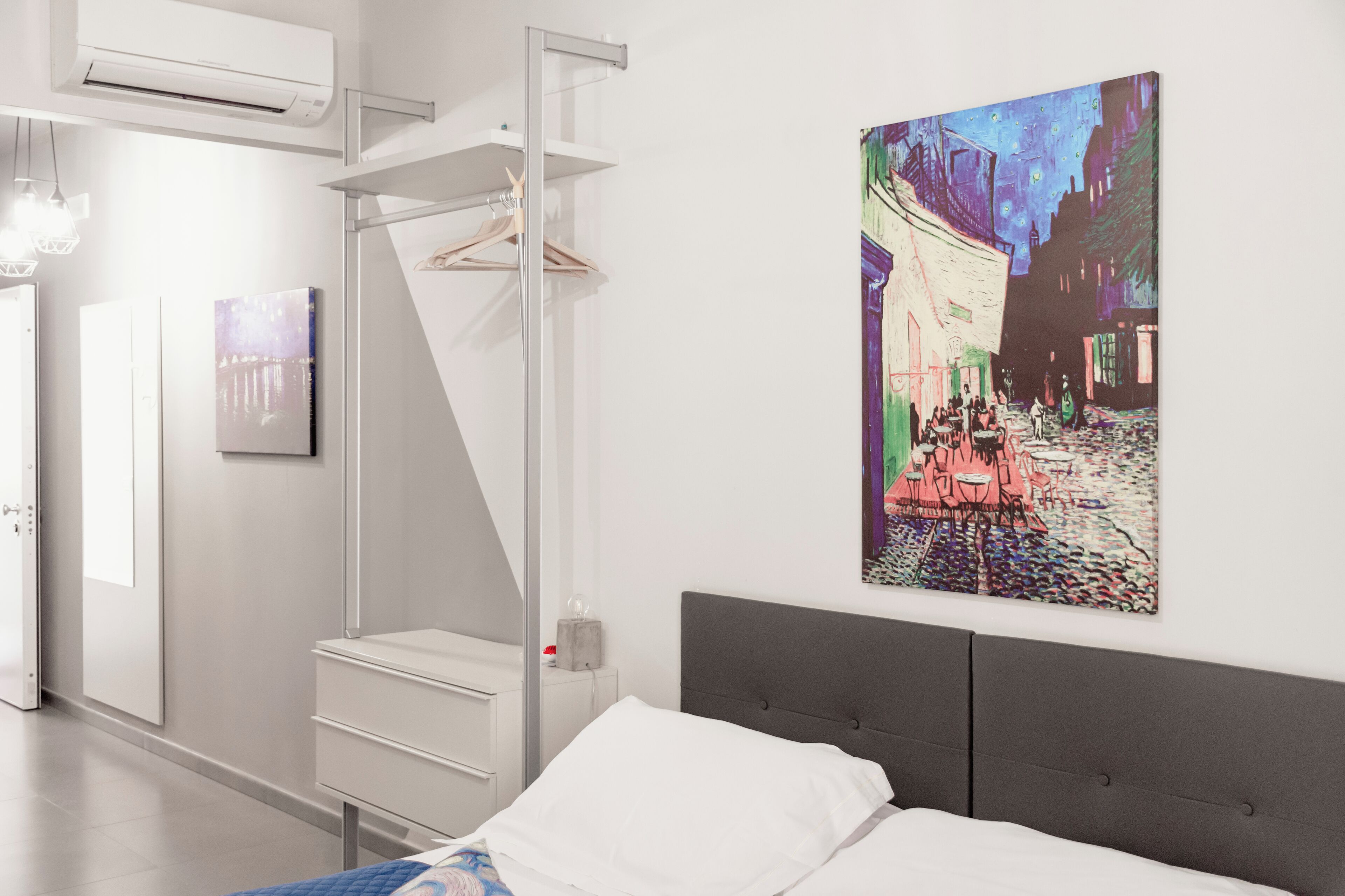 Quarto de hotel moderno com cama, guarda-roupa, cadeira suspensa e um quadro de uma cena urbana.