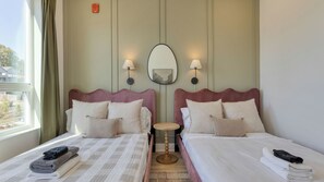 Quarto de hotel com duas camas, uma mesa redonda, um espelho e duas luminárias fixadas na parede.
