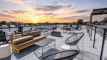 Terraço no telhado com sofá, cadeiras, mesas e um pérgola.