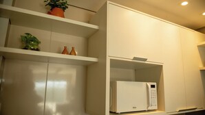 Cozinha com armários brancos, micro-ondas e prateleiras com objetos decorativos.