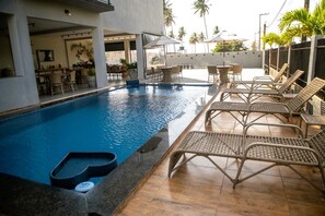 Uma piscina com espreguiçadeiras e guarda-sóis, cercada por um espaço de estar com piso cerâmico.