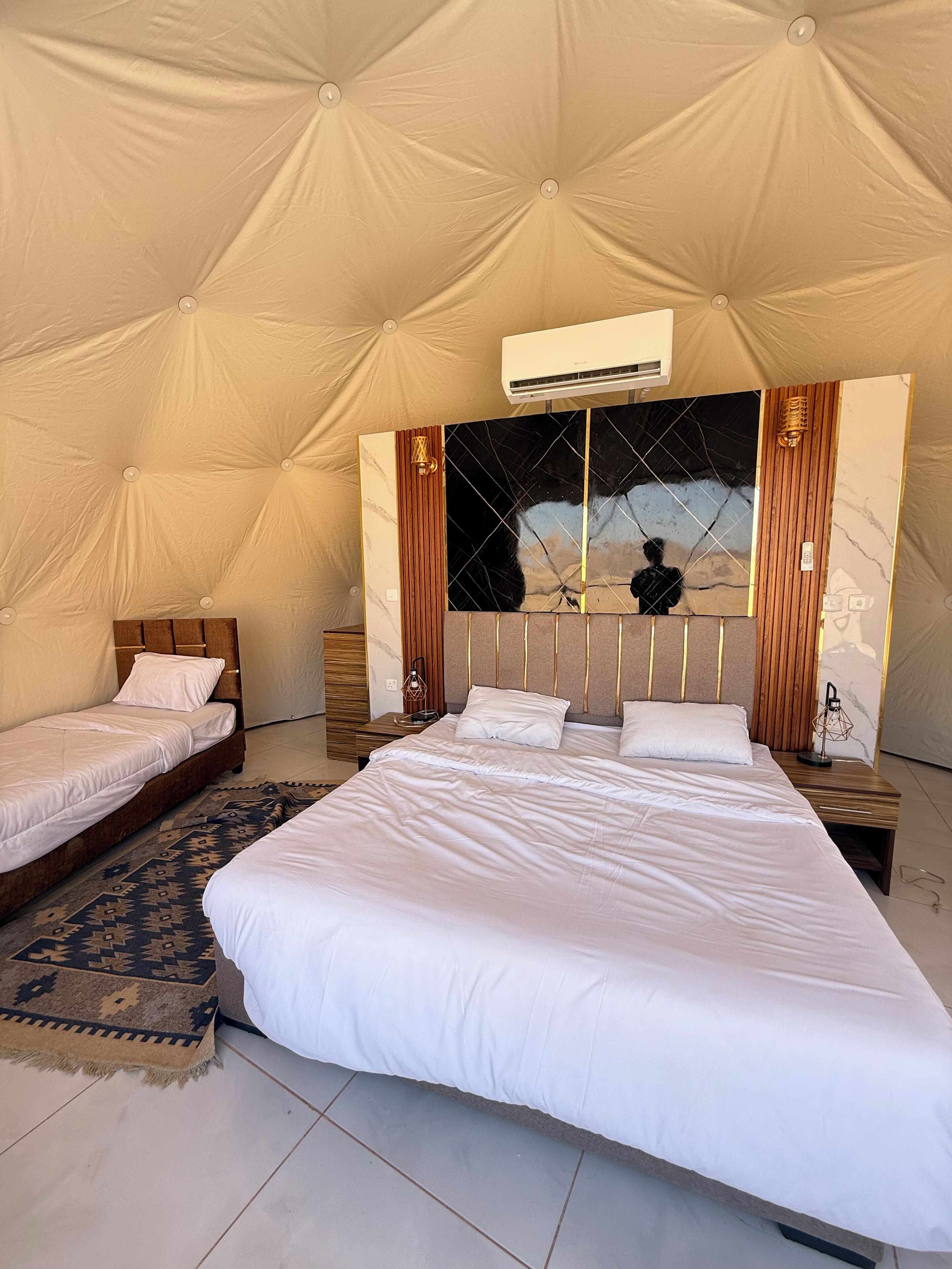 Um quarto no estilo de tenda espaçoso, com uma cama grande, duas camas menores e ar condicionado fixado na parede.