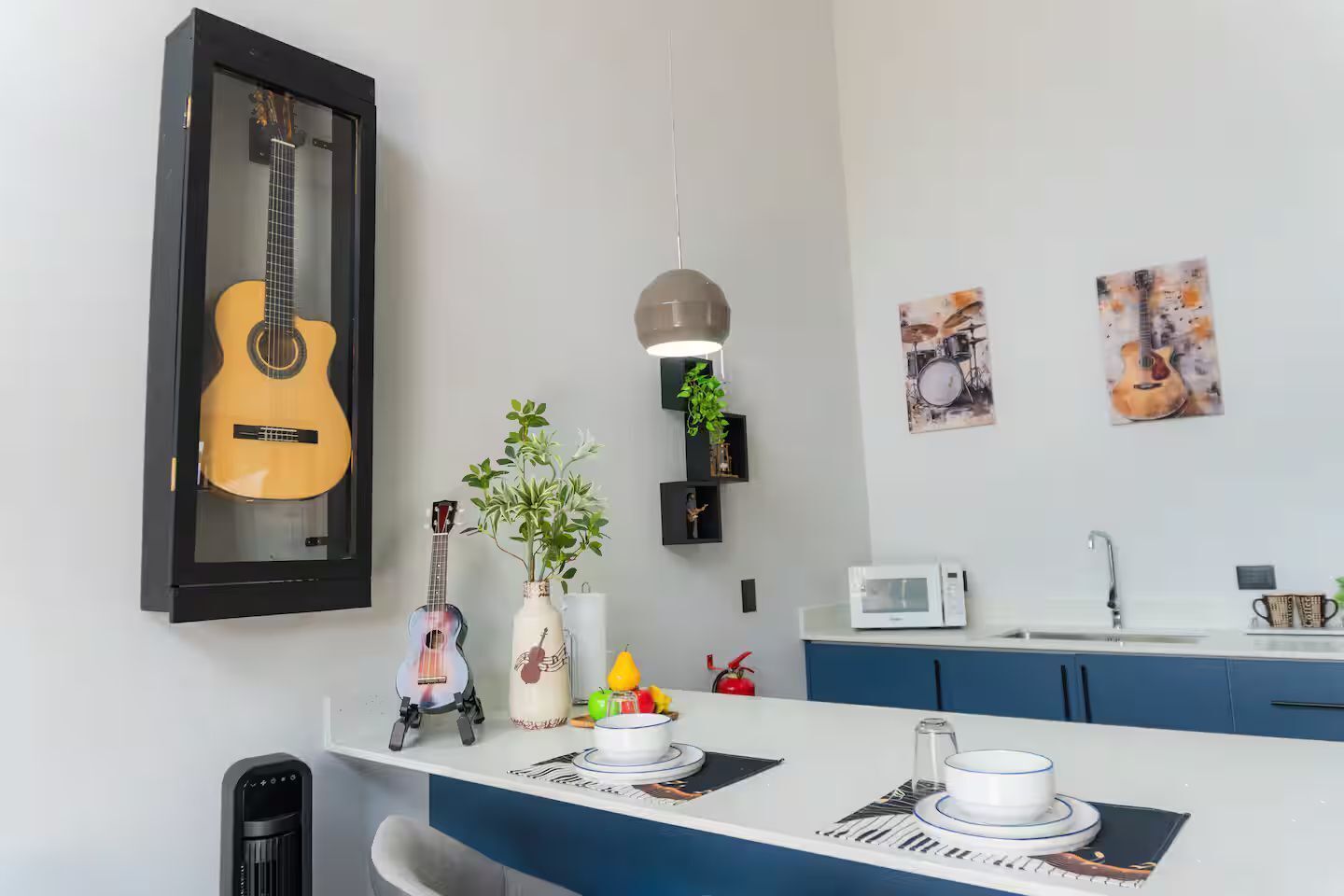 Cozinha moderna com uma guitarra, micro-ondas e área de jantar com uma mesa branca posta para dois.