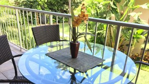 Mesa de vidro redonda com cadeira de fibra natural e um vaso com planta numa varanda.