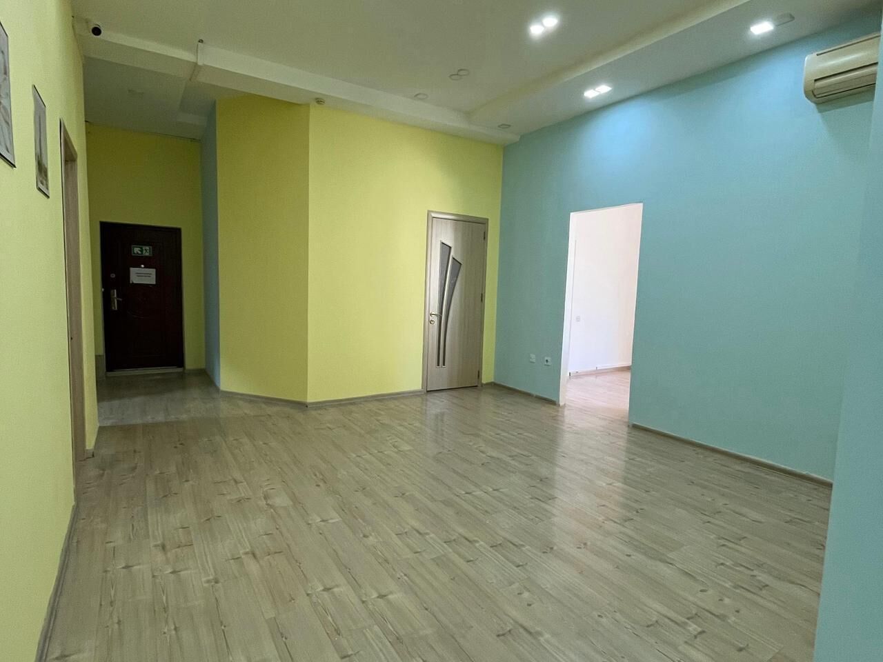 Um corredor com piso de madeira, uma porta e uma parede com interruptor de luz.