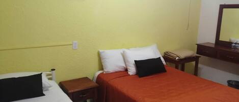 Quarto de hotel com duas camas, uma mesa de cabeceira de madeira, uma escrivaninha com um espelho e um quadro na parede.