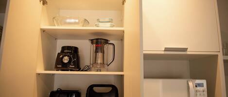 Uma cozinha com micro-ondas branco, máquina de café preta, liquidificador e um recipiente de vidro na prateleira.