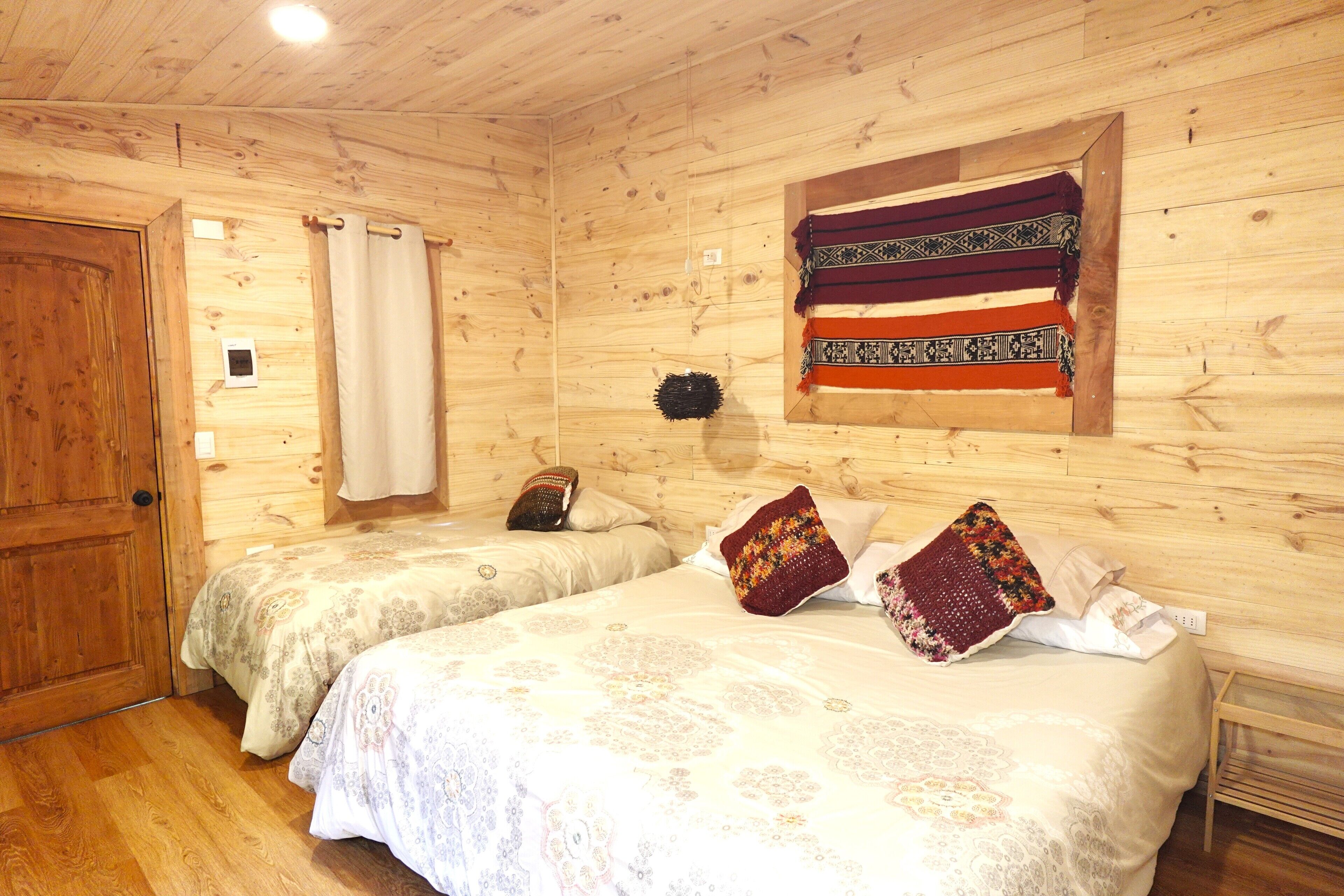 Quarto de cabana de madeira com duas camas, uma porta de madeira e cortina fixada na parede.