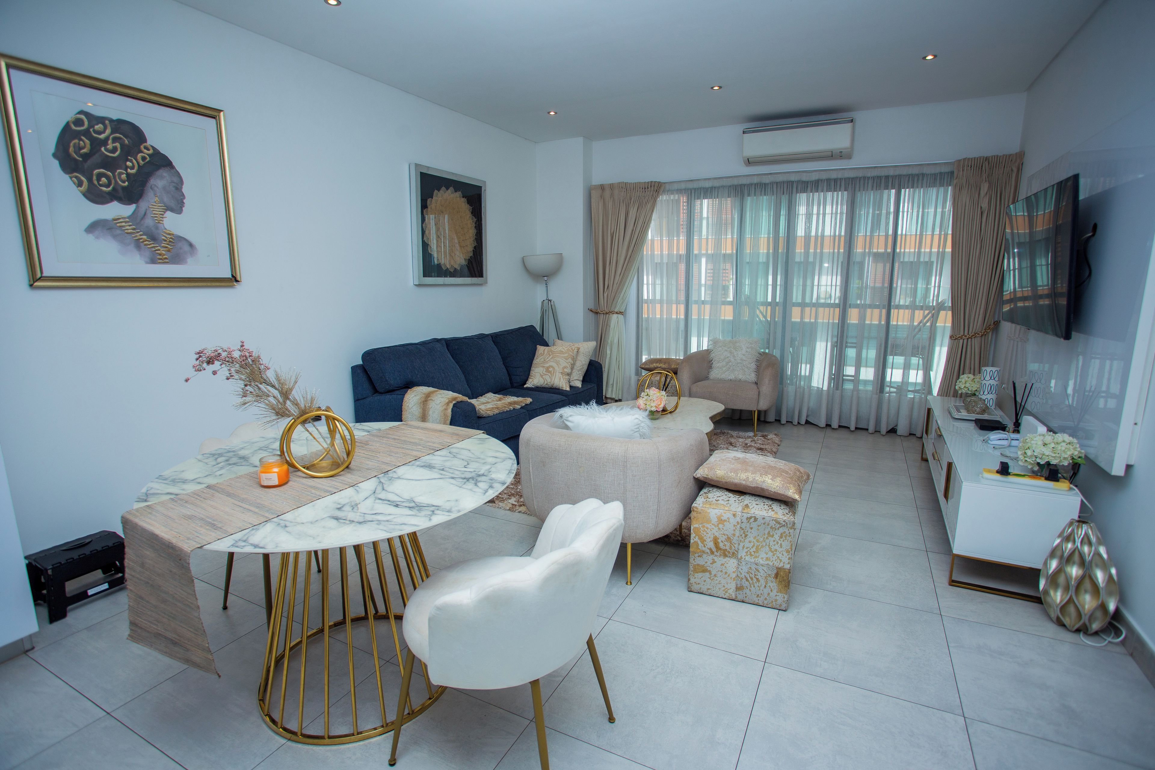 Uma sala de estar moderna com sofá, banqueta, mesa de jantar e televisão fixada na parede.