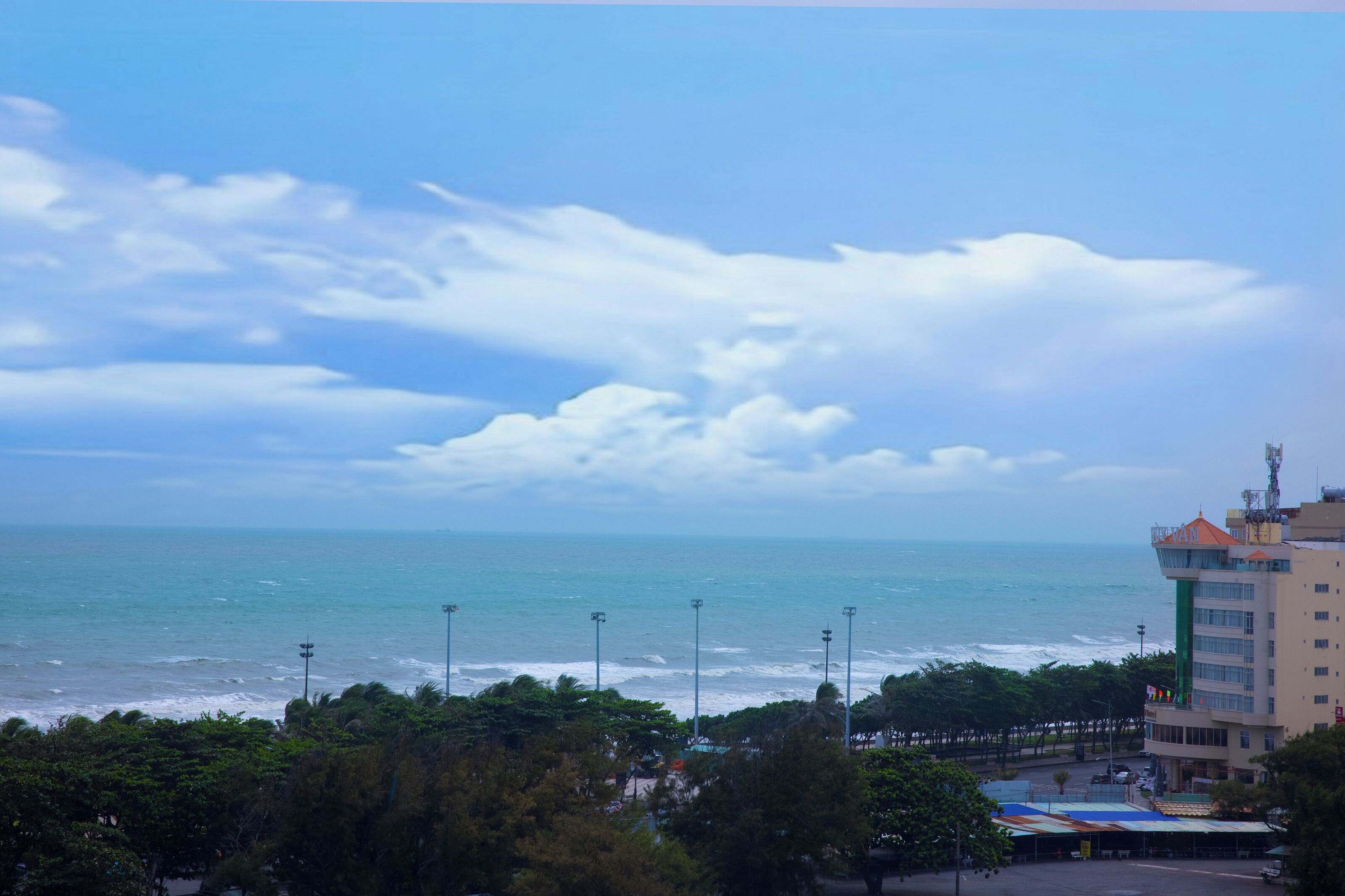 Vista costeira com um edifício que inclui uma torre de controle, área de estacionamento e vista do mar.
