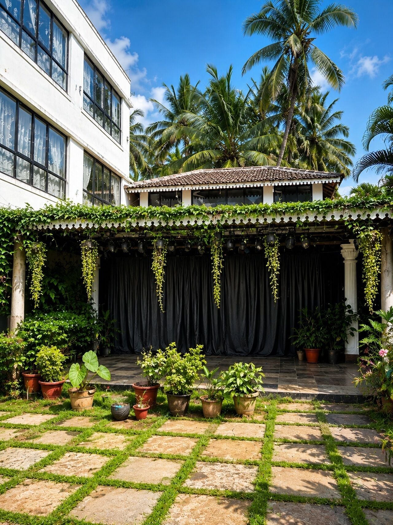 Um pátio com área de estar coberta, plantas em vasos e um edifício com janelas amplas.