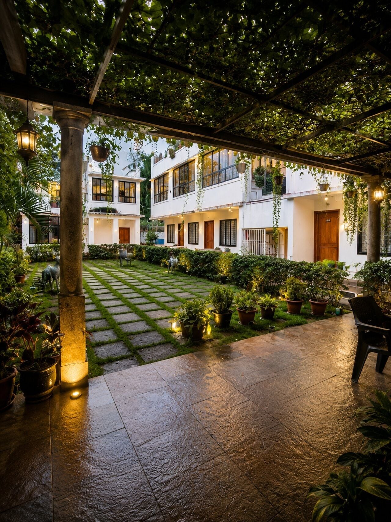 Pátio com calçada pavimentada, plantas em vasos e uma estrutura de pérgola.