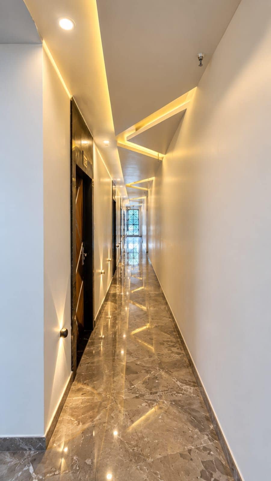Um corredor moderno com piso de mármore polido, iluminação embutida e um caminho reto até uma porta.
