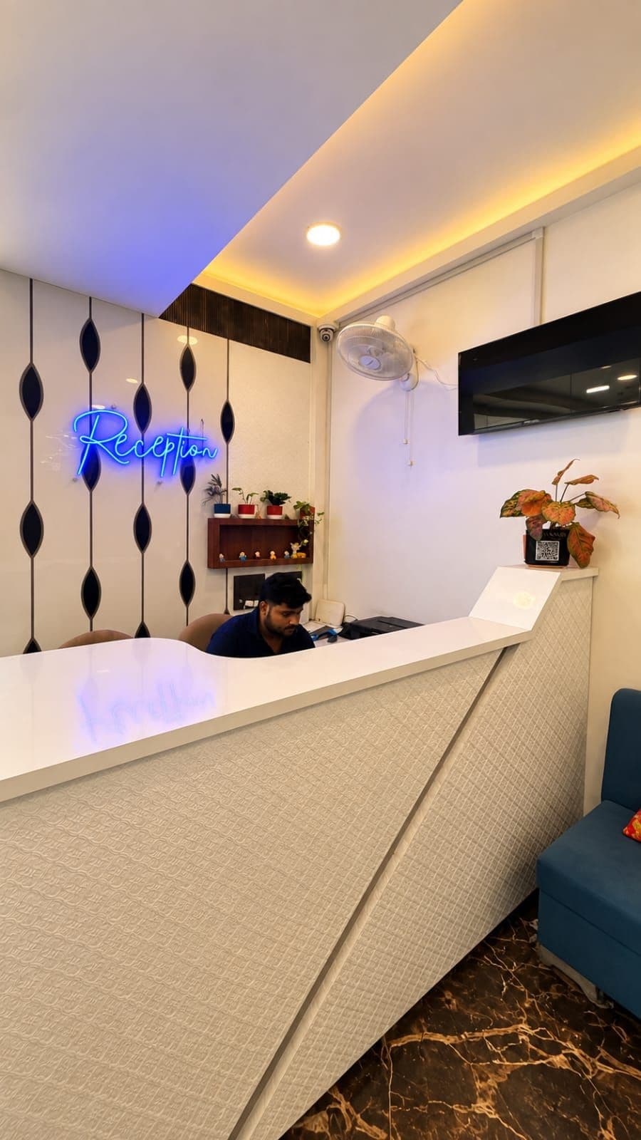 Uma mesa de recepção com uma placa de neon, uma televisão montada e uma planta na parede.