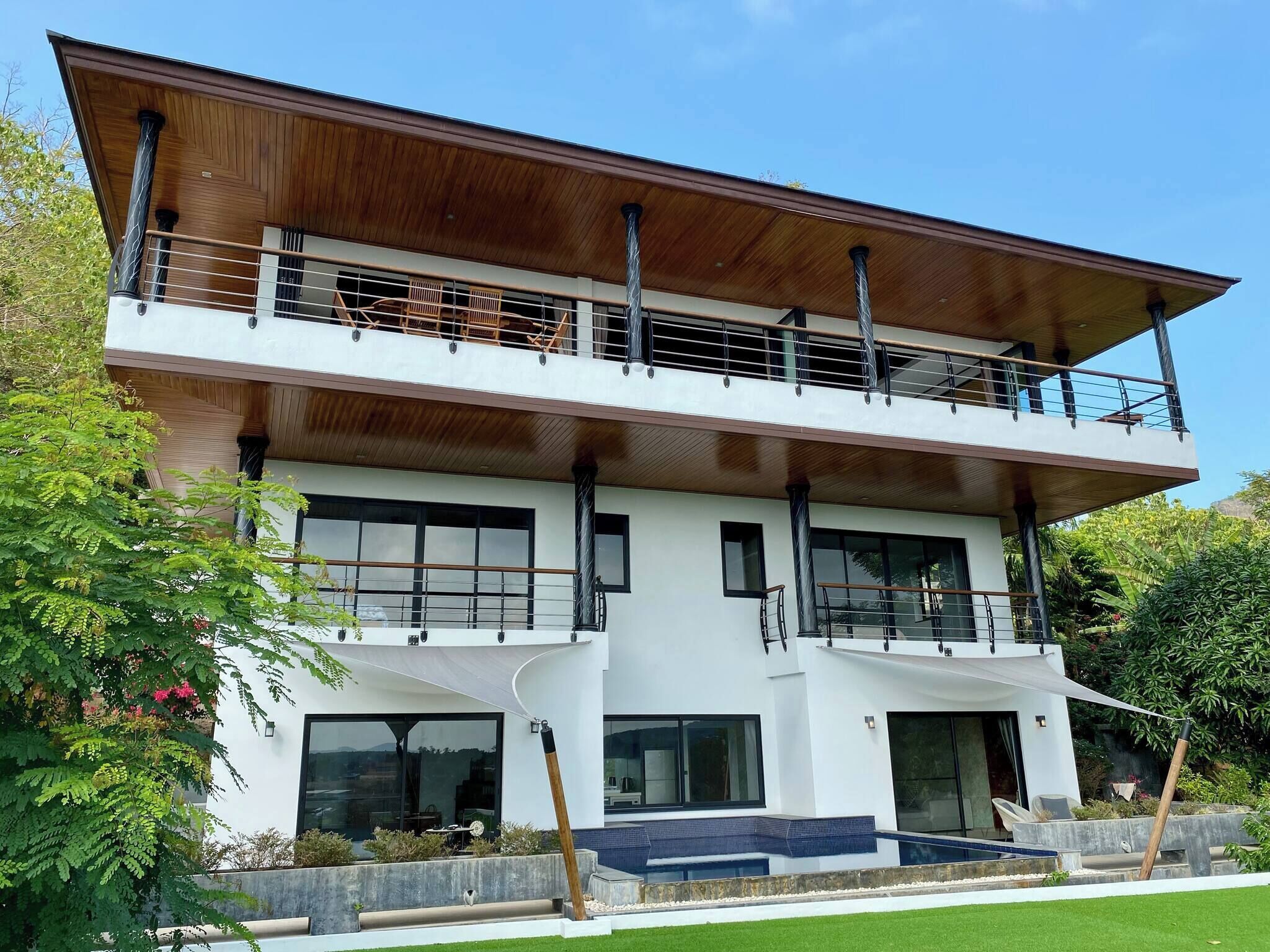 Uma casa moderna de dois andares com telhado de madeira, janelas amplas e uma varanda.