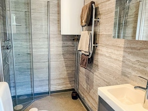 Casa de banho moderna com cabine de duche em vidro, lavatório branco e um porta-toalhas com toalhas.