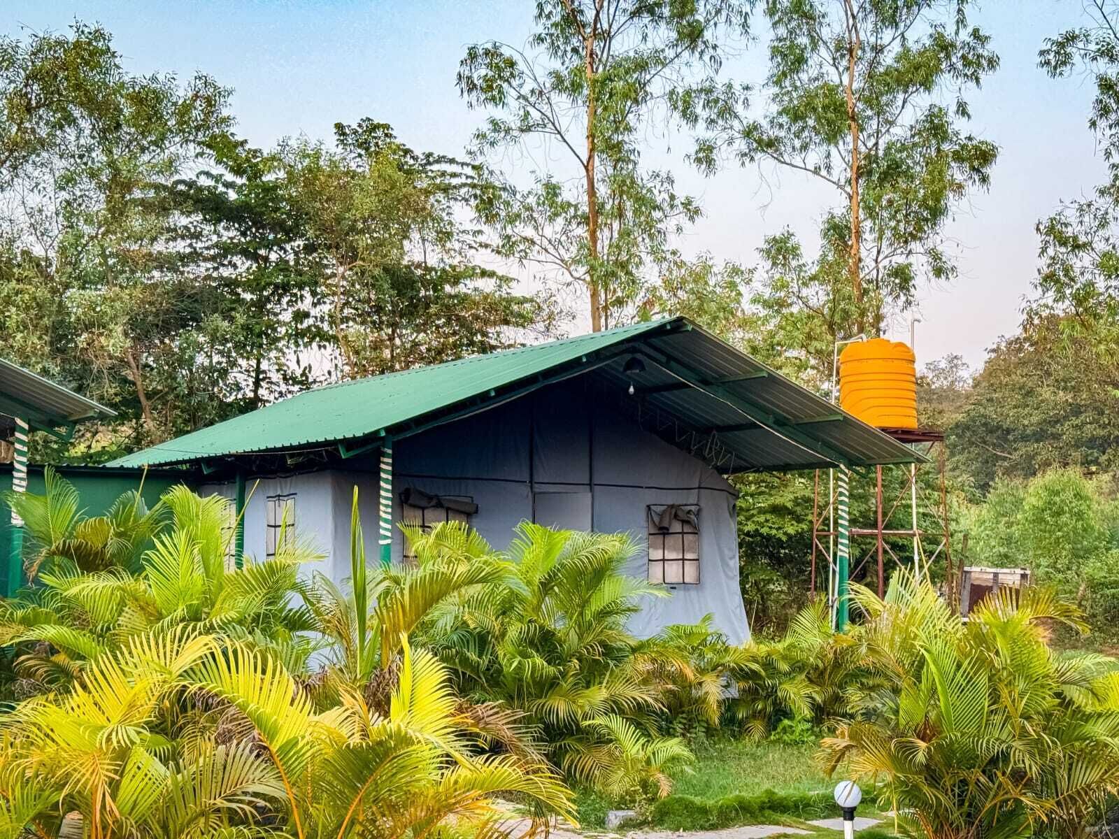 Uma casa pequena, térrea, com telhado verde e um reservatório de água à direita.