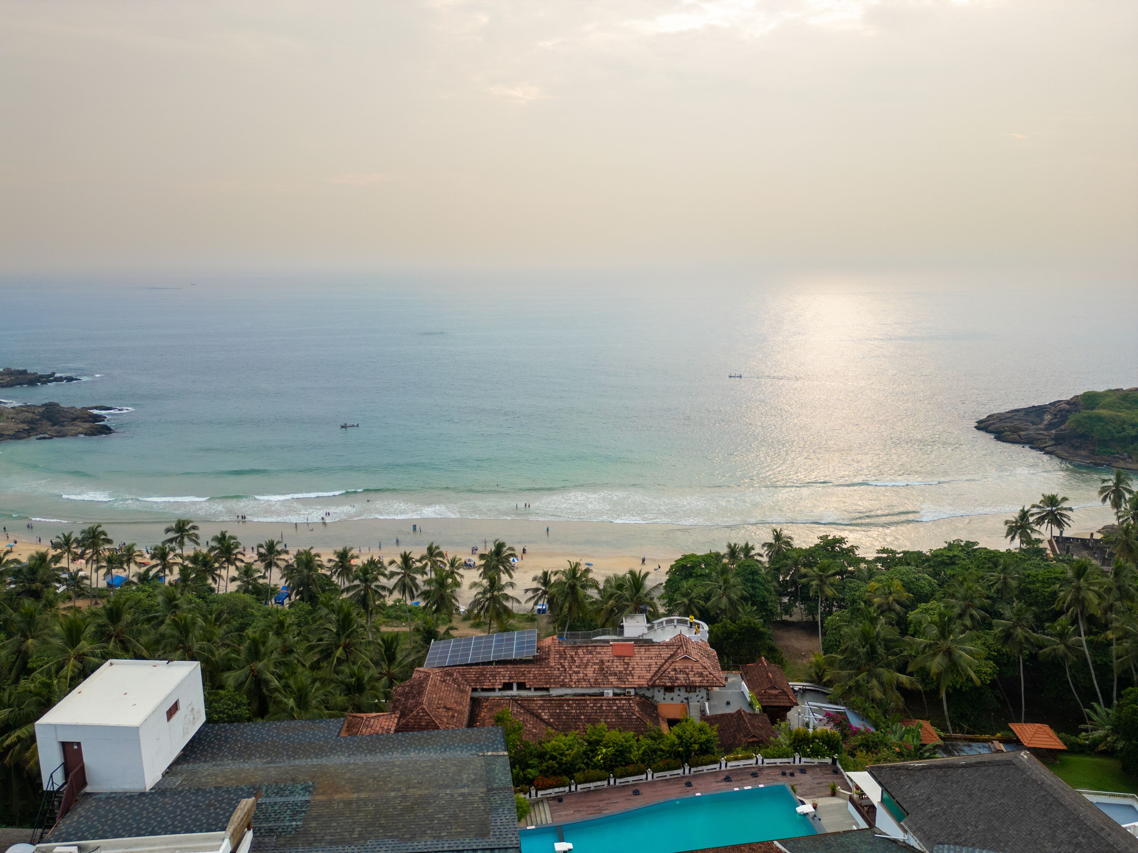 Vista costeira com praia, palmeiras e um edifício com piscina.