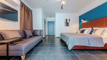 Quarto de hotel moderno com sofá, cama, televisão de tela plana e luminária embutida no teto.