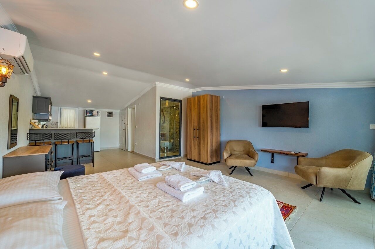 Quarto de hotel com uma cama grande, uma escrivaninha com cadeiras, televisão e guarda-roupa.