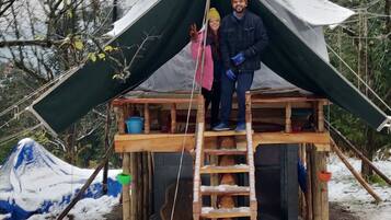 Uma estrutura de madeira com telhado cónico e uma escada que dá acesso à entrada, sobre um terreno coberto de neve.