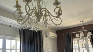 Quarto de hotel com duas camas, um lustre, ar condicionado e cortinas.
