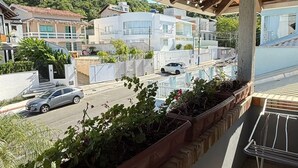 Uma varanda com teto de madeira, plantas em vasos e vista para edifícios e uma rua.