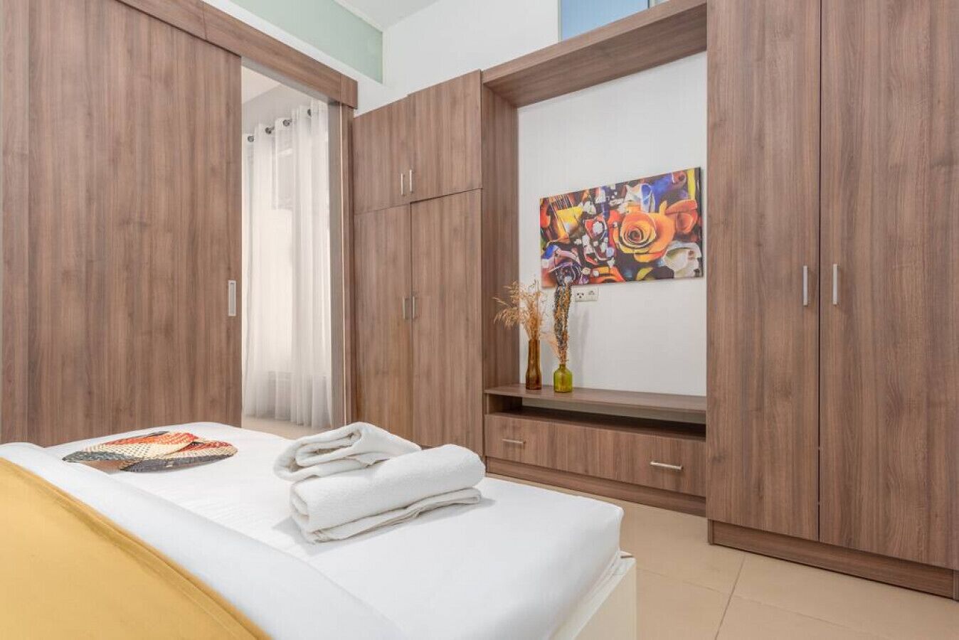 Quarto de hotel com uma cama, um quadro na parede e uma pequena mesa com um vaso.