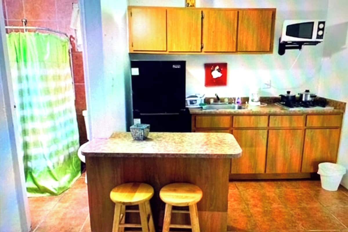 Cozinha com armários de madeira, geladeira preta, micro-ondas e uma pequena ilha com banquetas.