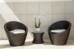 Duas cadeiras de vime com almofadas brancas e uma pequena mesa com uma orquídea em vaso no meio.