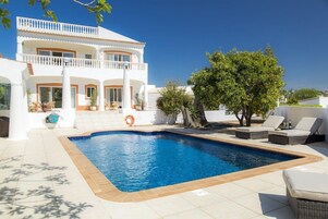 Uma casa de dois andares com piscina, área de estar externa e uma árvore.