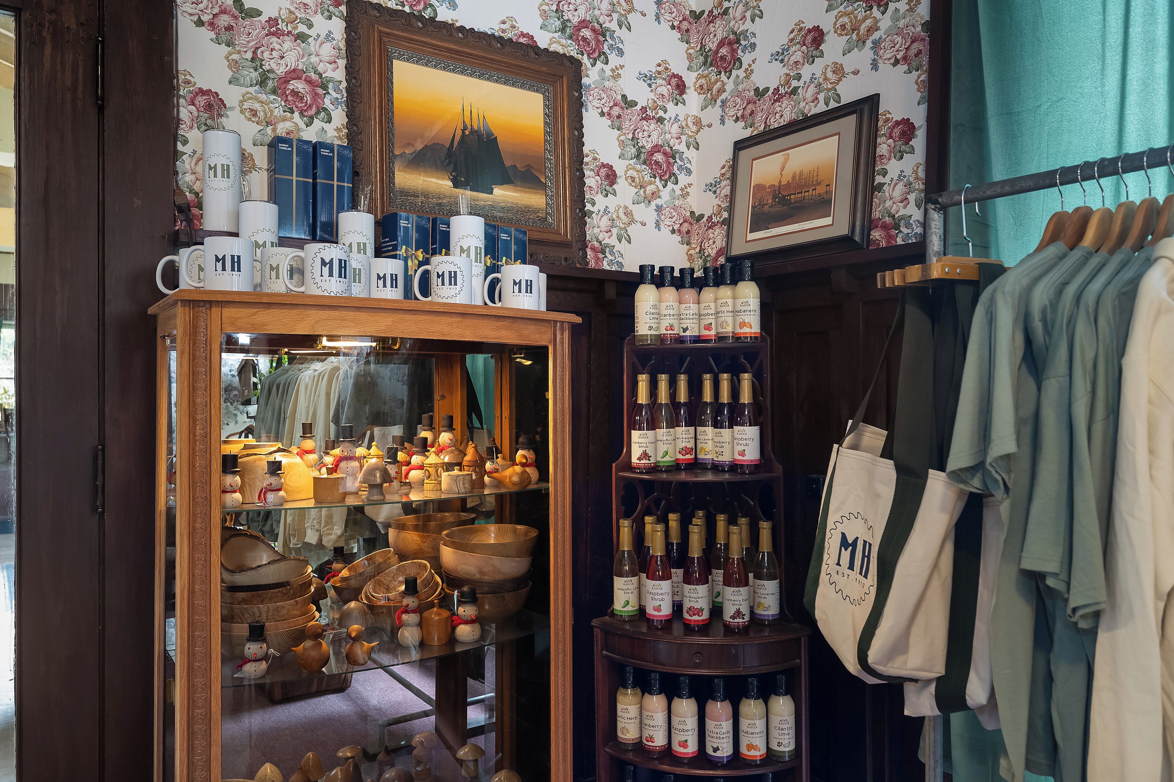 Interior de um hotel boutique com uma exposição de canecas, garrafas e araras de roupa.
