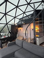Um interior moderno com teto de vidro geométrico, um sofá, uma mesa e uma escada.