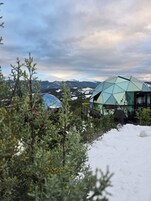 Uma estrutura moderna em cúpula de vidro com vista para montanhas cobertas de neve ao fundo.