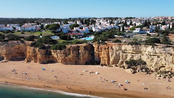 Uma vila costeira com praia, falésias rochosas e edifícios brancos.