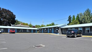 Um motel com edifícios de dois andares, um estacionamento e um carro vermelho estacionado no local.