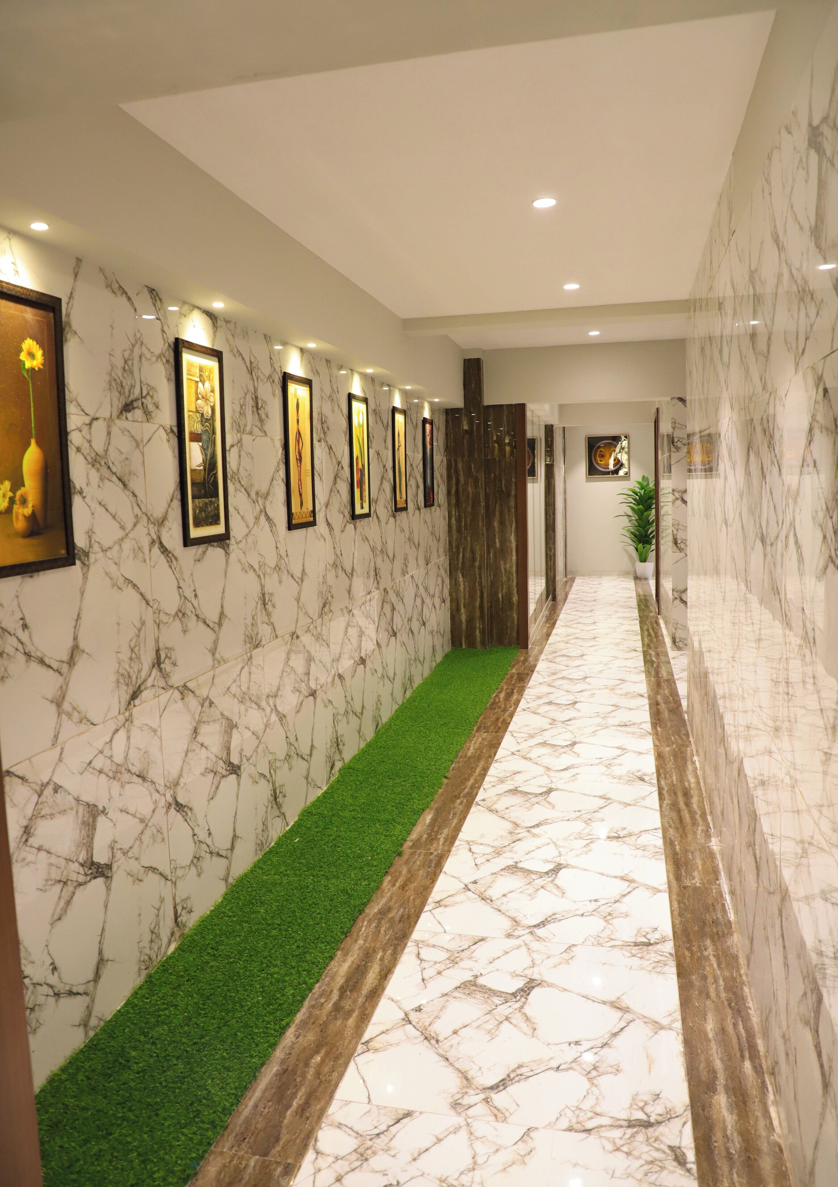 Um corredor com paredes de mármore, obras de arte emolduradas e um caminho de grama sintética verde.