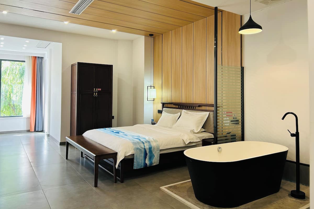 Quarto de hotel moderno com cama, um banquinho, banheira e guarda-roupa.