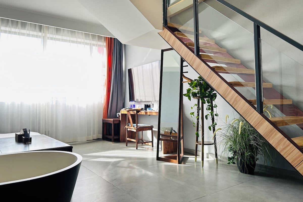 Quarto de hotel moderno com escada, área de refeições e uma grande janela com cortinas.