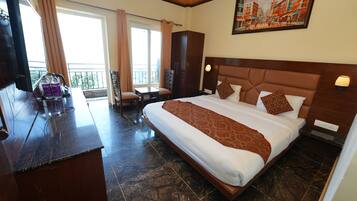 Quarto de hotel com cama grande, secretária com computador, cadeira, guarda-roupa e varanda com cortinas.