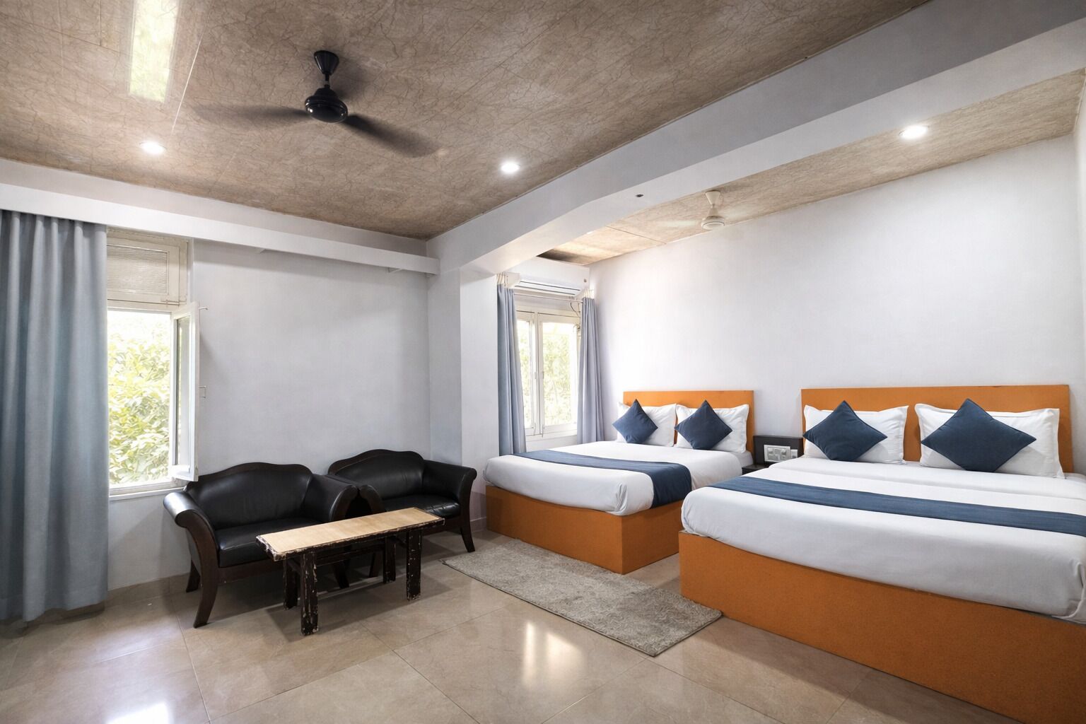 Quarto de hotel com duas camas, um sofá, uma mesinha e um ventilador de teto.