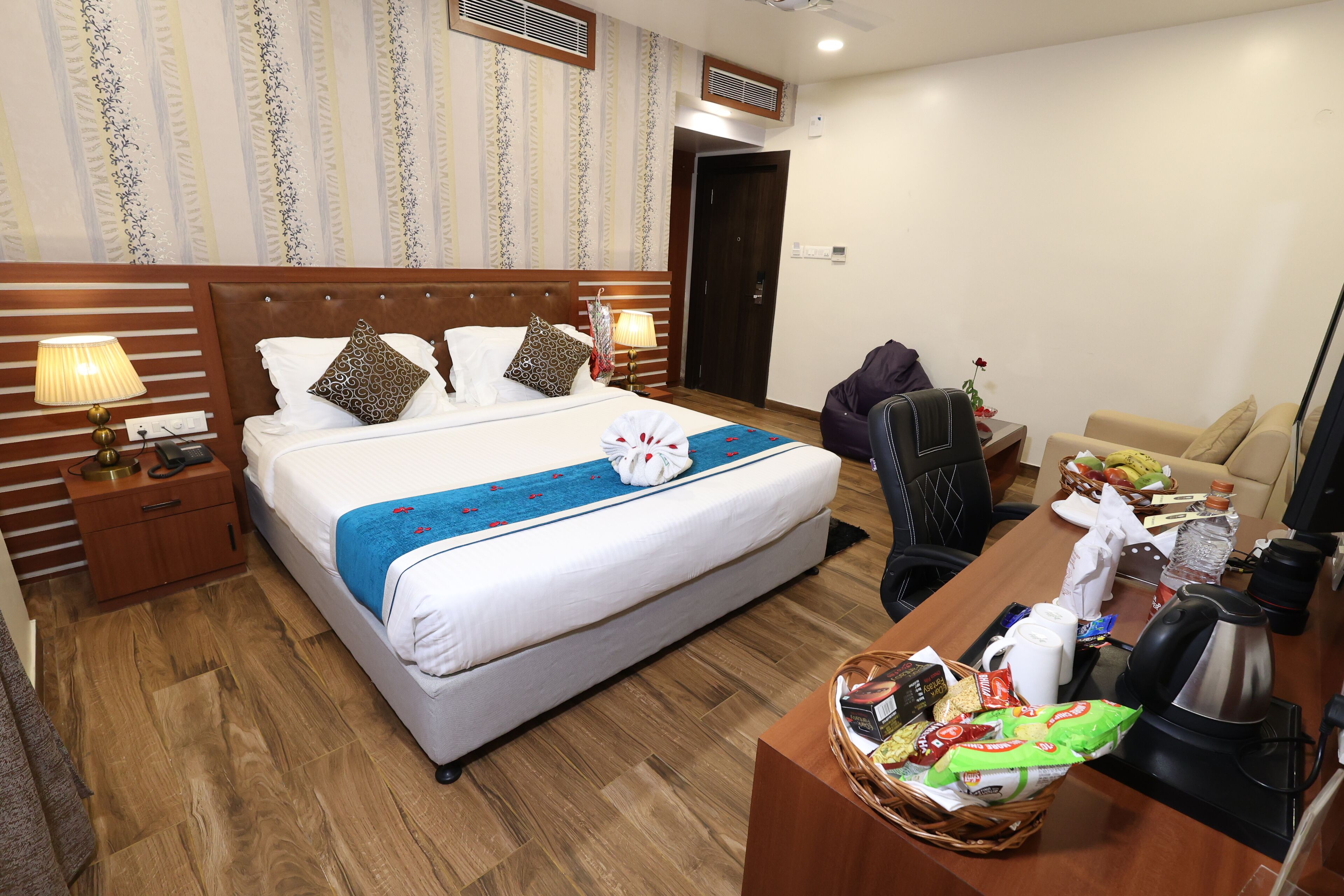 Quarto de hotel com uma cama grande, uma escrivaninha com cafeteira, um cesto de lanches e uma cadeira.