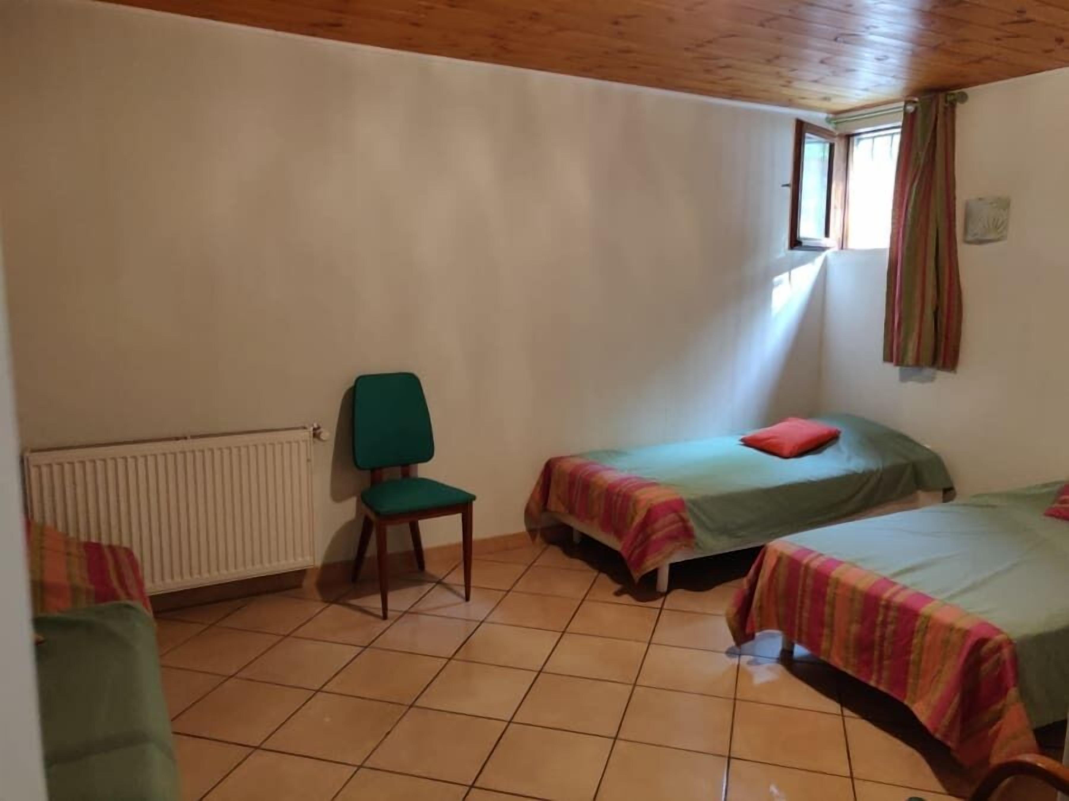 Quarto pequeno e simples com duas camas, uma cadeira e um radiador.
