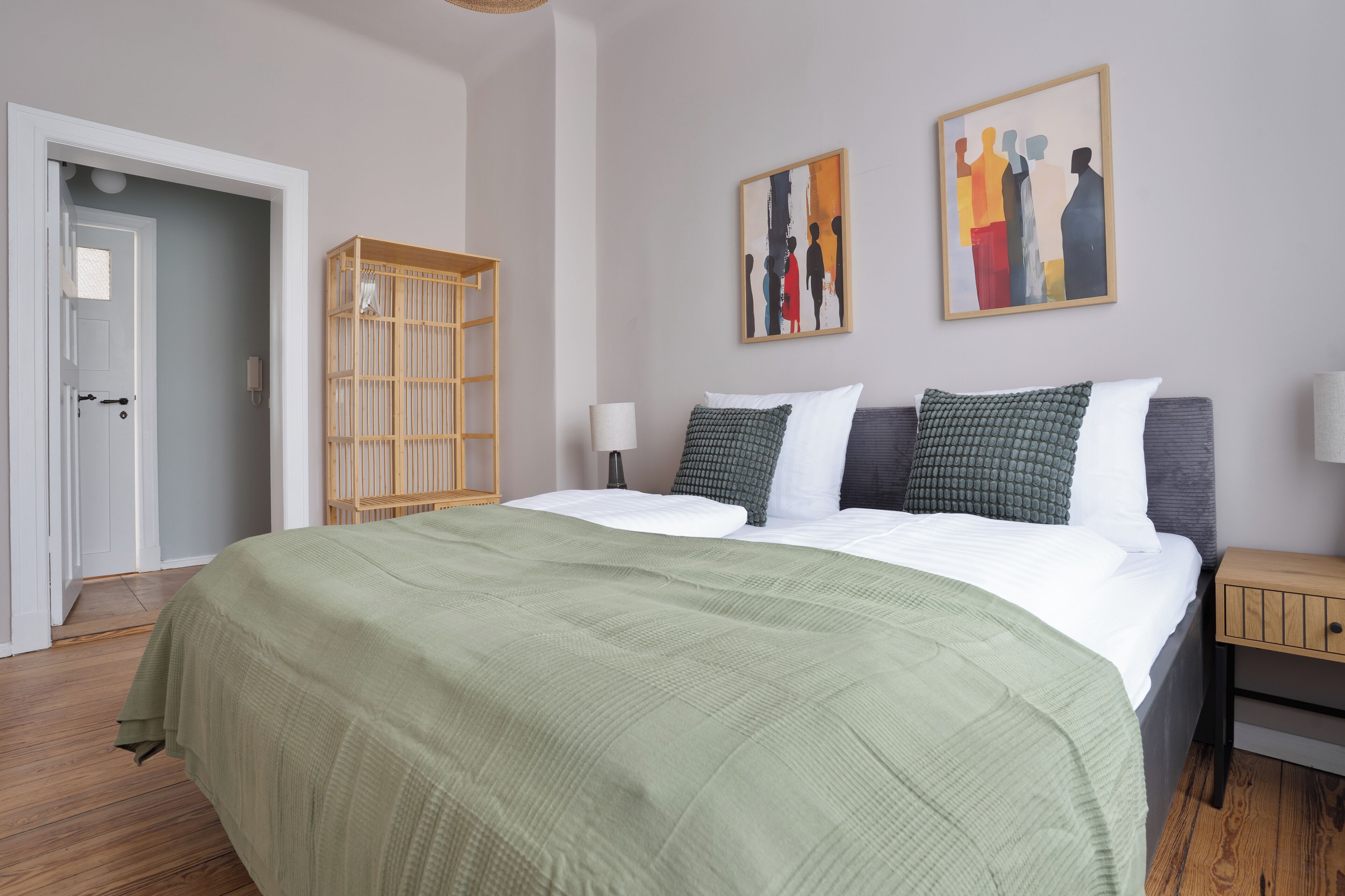 Um quarto com uma cama grande, duas mesas de cabeceira, um guarda-roupa de madeira e duas pinturas abstratas na parede.
