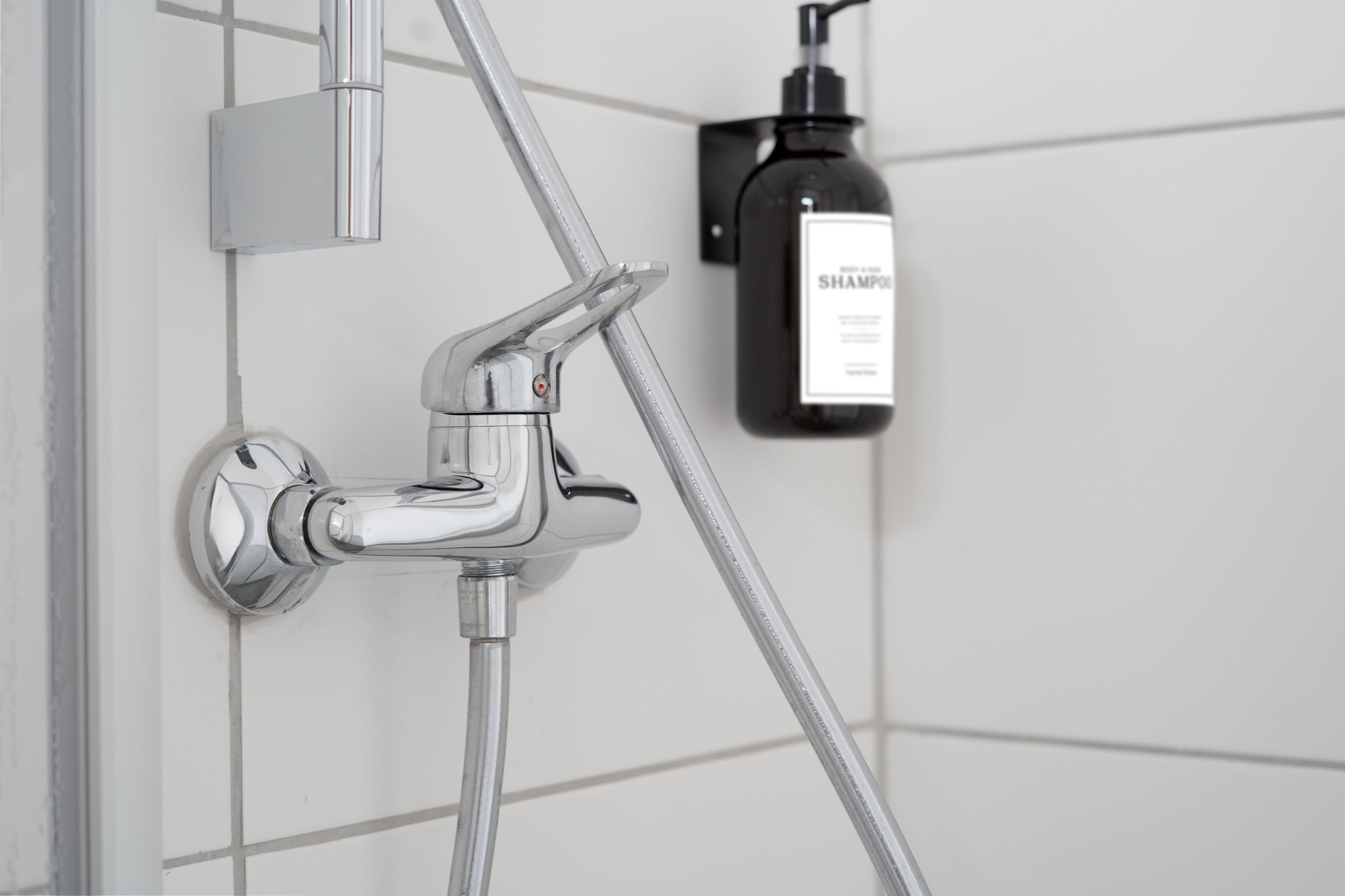 Um banheiro com chuveiro cromado e uma garrafa de shampoo na parede.