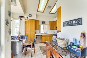 Cozinha com armários de madeira, placa indicando bar de café e área de refeições com mesa e cadeiras.